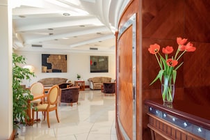 Um hall amplo com balcão de atendimento em madeira, um vaso com flores vermelhas e uma área de estar com sofás e cadeiras.