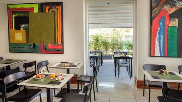 Uma sala de jantar moderna com mesas e cadeiras, pinturas abstratas grandes nas paredes e vista para o verde lá fora.