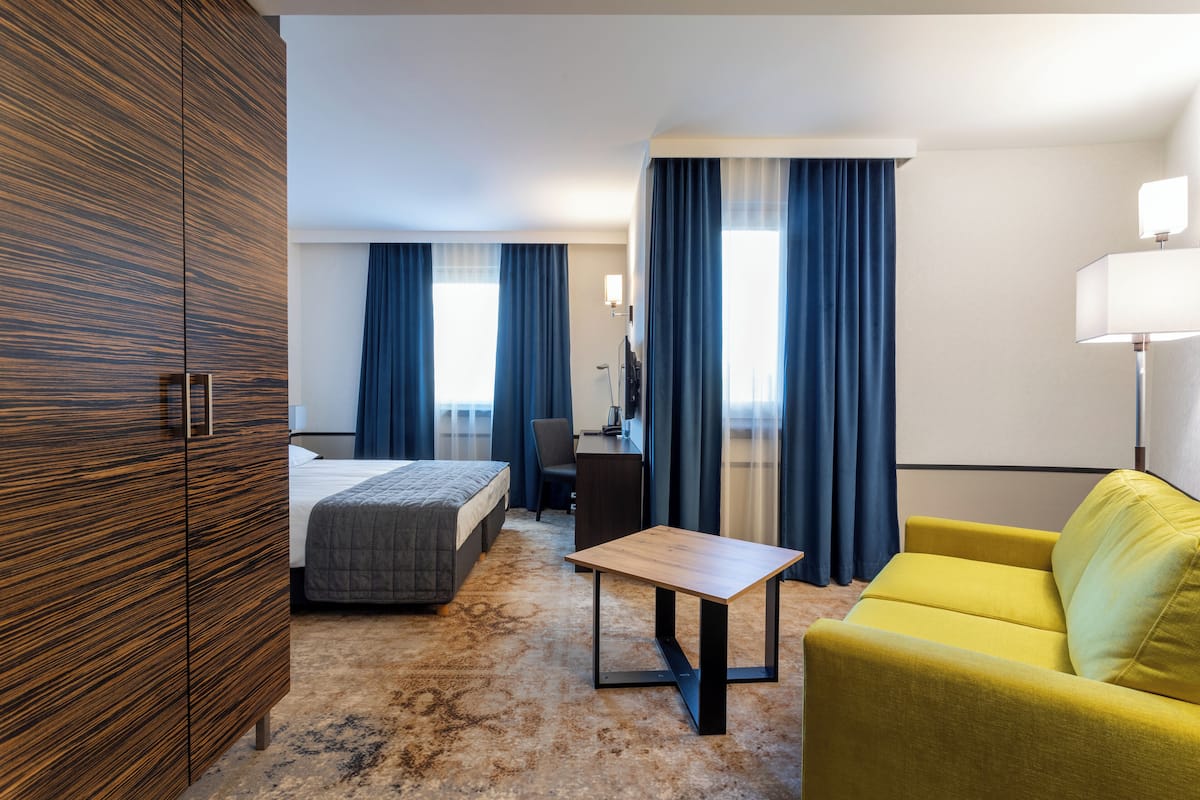 Quarto de hotel com cama, escrivaninha, cadeira, sofá e guarda-roupa.