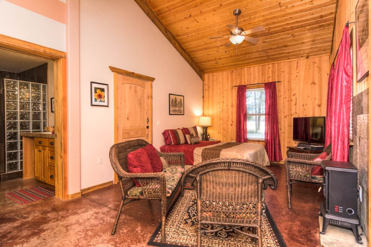 Interior acolhedor de uma cabana com teto de madeira, móveis de vime, uma televisão e uma lareira.