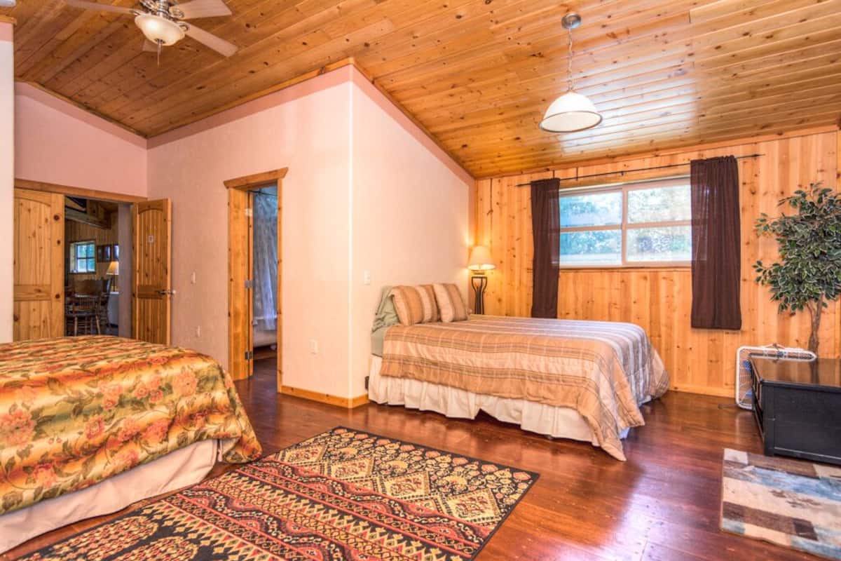 Um quarto acolhedor com duas camas, teto de madeira, uma janela grande e uma planta.