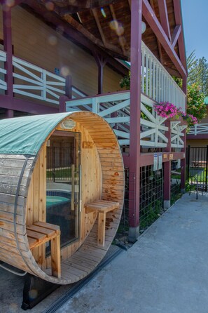 Uma sauna de madeira com telhado curvo, um banco no interior e vista para um edifício com varanda e vedação.