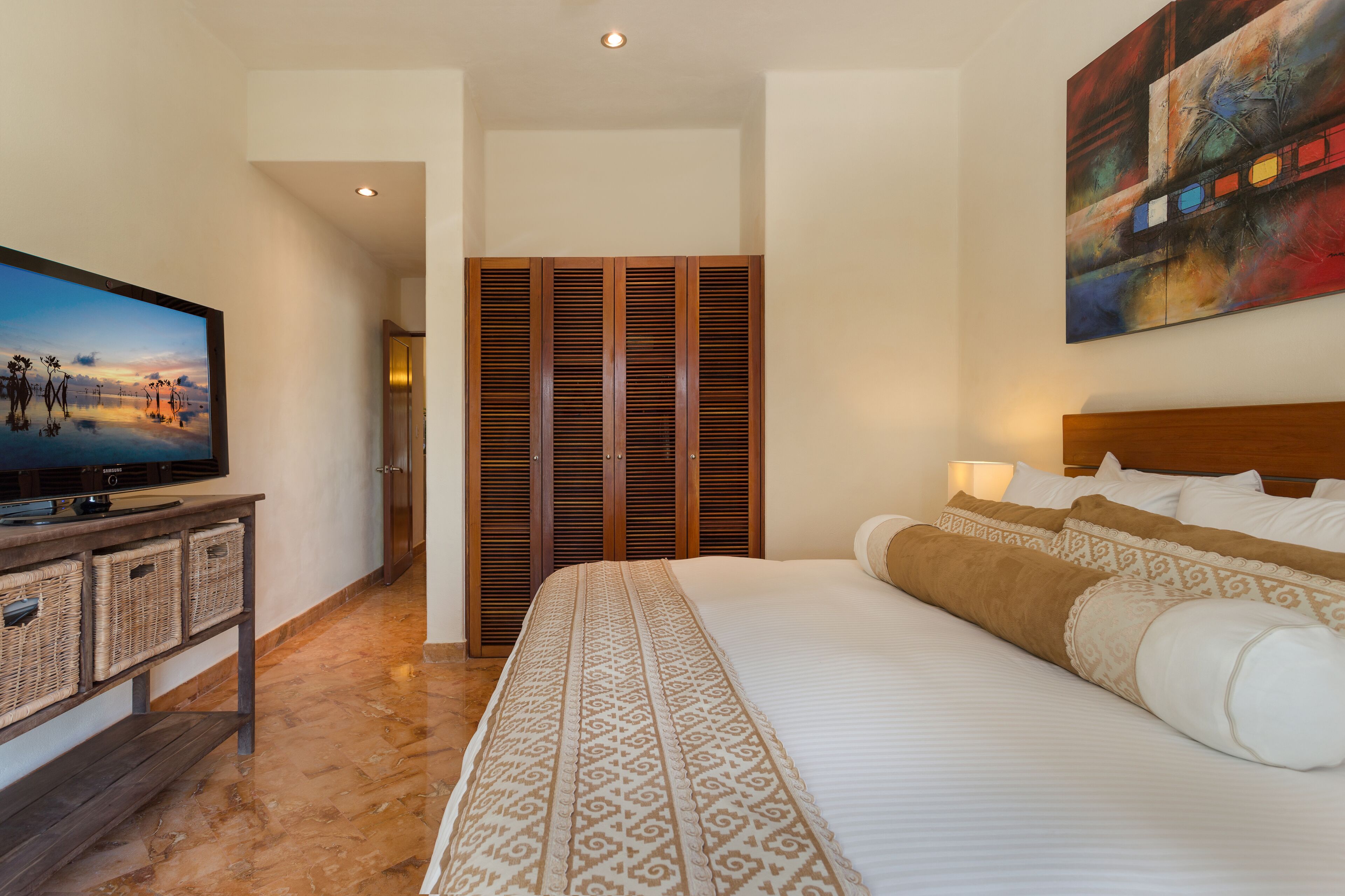 Quarto de hotel com cama, televisão, guarda-roupa e um quadro na parede.