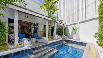 Uma área de piscina moderna ao ar livre, com zona de estar coberta, degraus para acesso à piscina e vegetação exuberante.