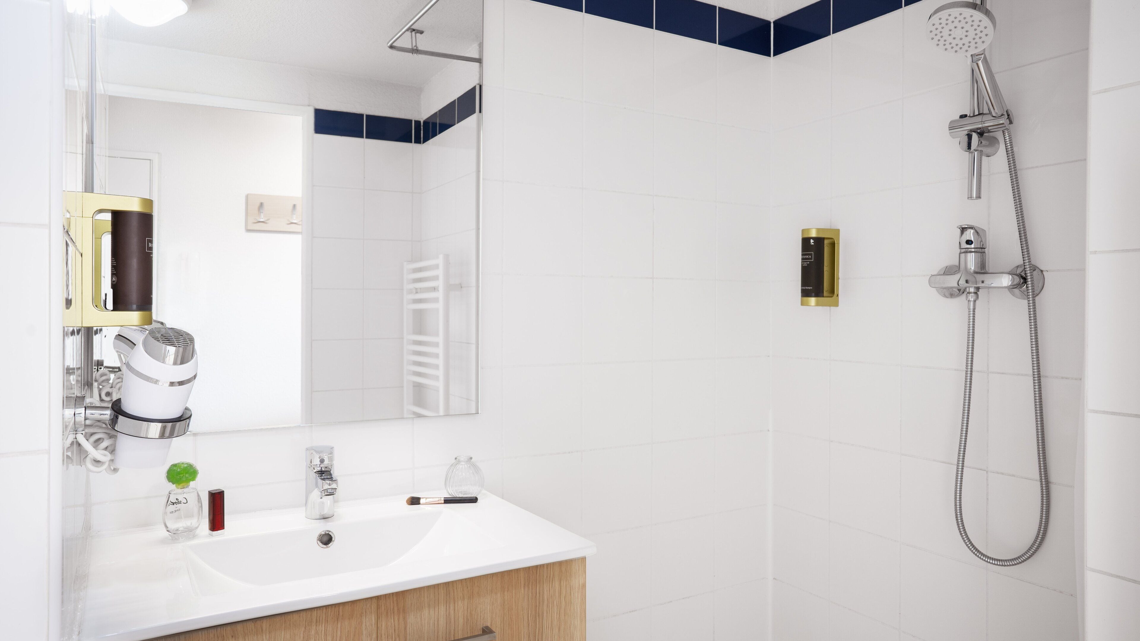 Casa de banho moderna com lavatório branco, espelho, chuveiro manual e barra de toalhas.