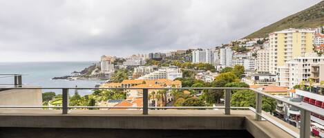 Uma varanda com vista para um horizonte costeiro, incluindo edifícios e o mar.