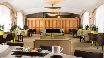 Um hall de hotel espaçoso com uma grande área de estar, uma televisão e uma mesa de centro com um prato de comida e uma xícara de café.