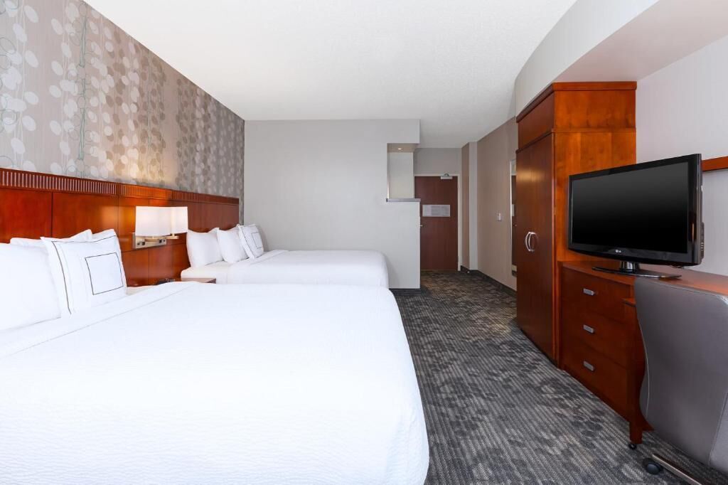 Quarto de hotel com duas camas, televisão, secretária e guarda-roupa.