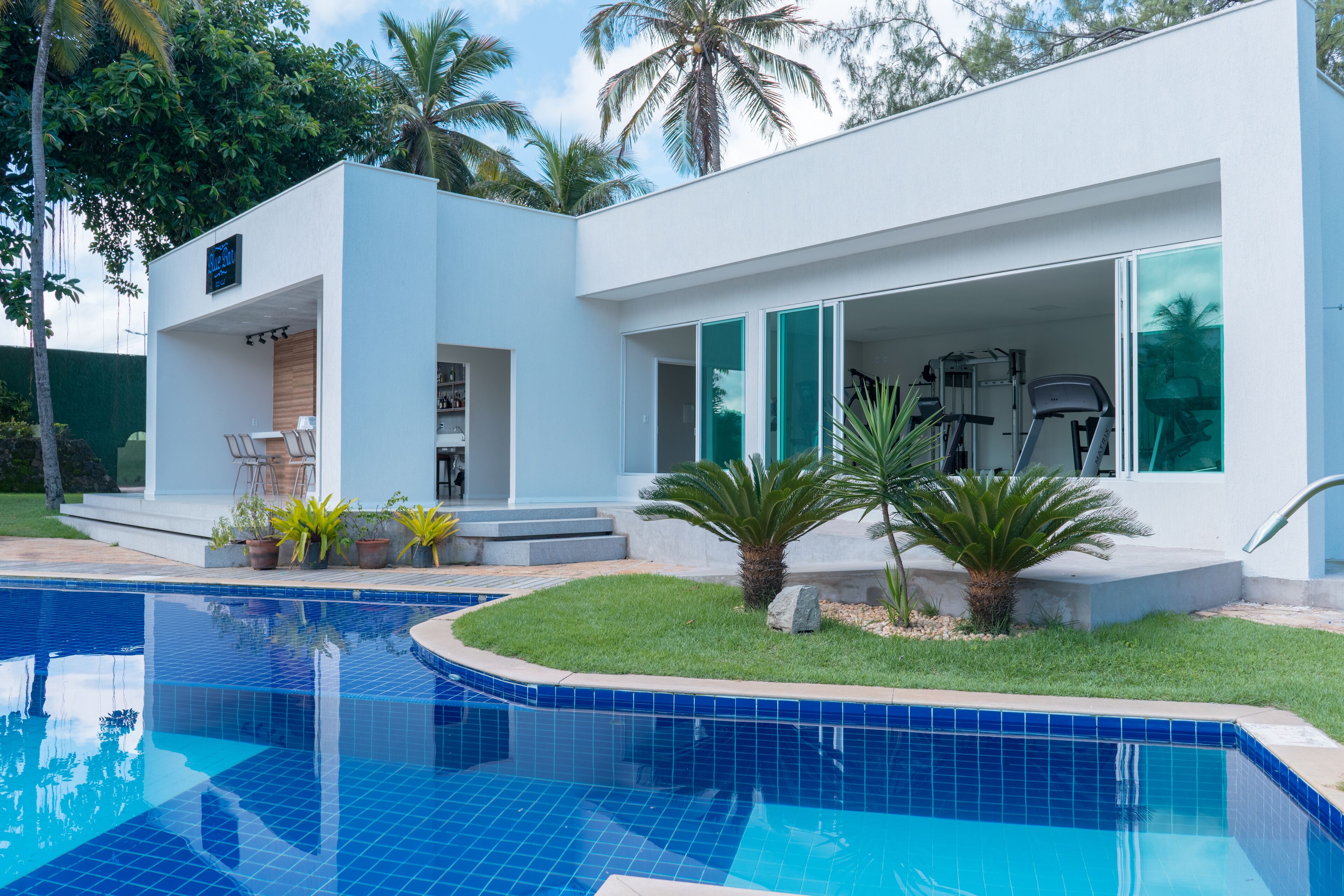 Uma casa moderna com piscina, um pátio com móveis de exterior e uma academia visível pelas janelas.