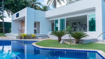 Uma casa moderna com piscina, um pátio com móveis de exterior e uma academia visível pelas janelas.