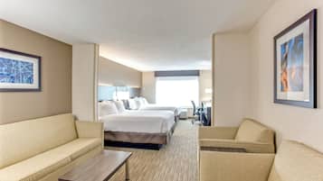 Quarto de hotel com cama, dois sofás, escrivaninha e uma grande janela.