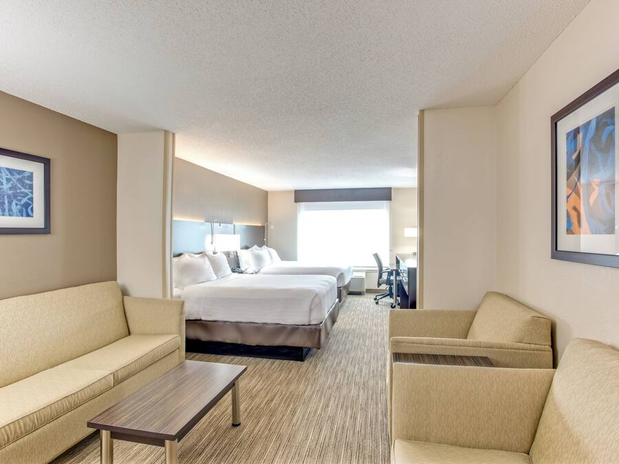 Quarto de hotel com cama, dois sofás, escrivaninha e uma grande janela.