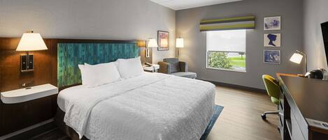Quarto de hotel com uma cama grande, mesas de cabeceira, uma escrivaninha e vista para o exterior.