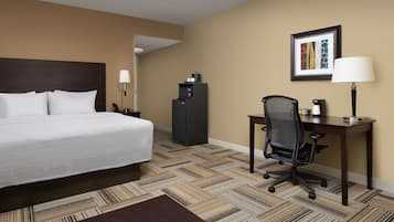 Quarto de hotel com cama, escrivaninha, cadeira e frigorífico.