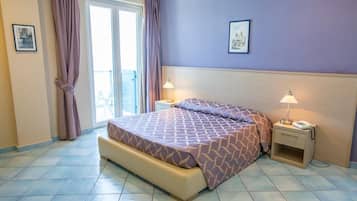 Quarto com cama, duas mesas de cabeceira, um criado-mudo, janela com cortinas e dois quadros na parede.