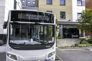 Um ônibus Volvo branco estacionado em frente a um edifício com a placa Holiday Inn Express.