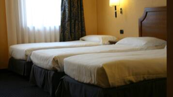 Quarto de hotel com duas camas de solteiro, mesa de cabeceira, luminária e janela com cortinas.