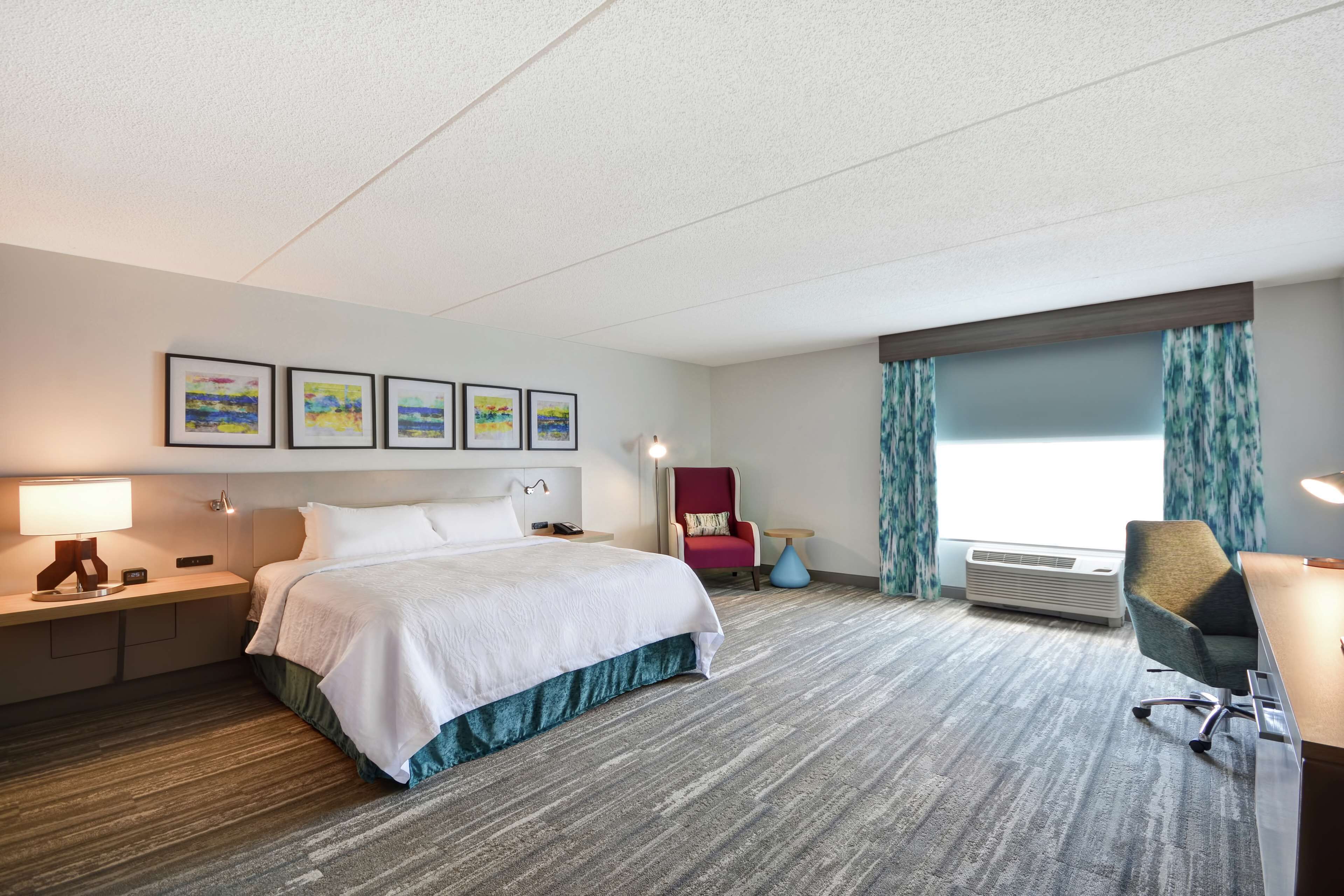 Quarto de hotel com cama, escrivaninha, cadeira e obras de arte na parede.