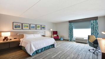 Quarto de hotel com cama, escrivaninha, cadeira e obras de arte na parede.