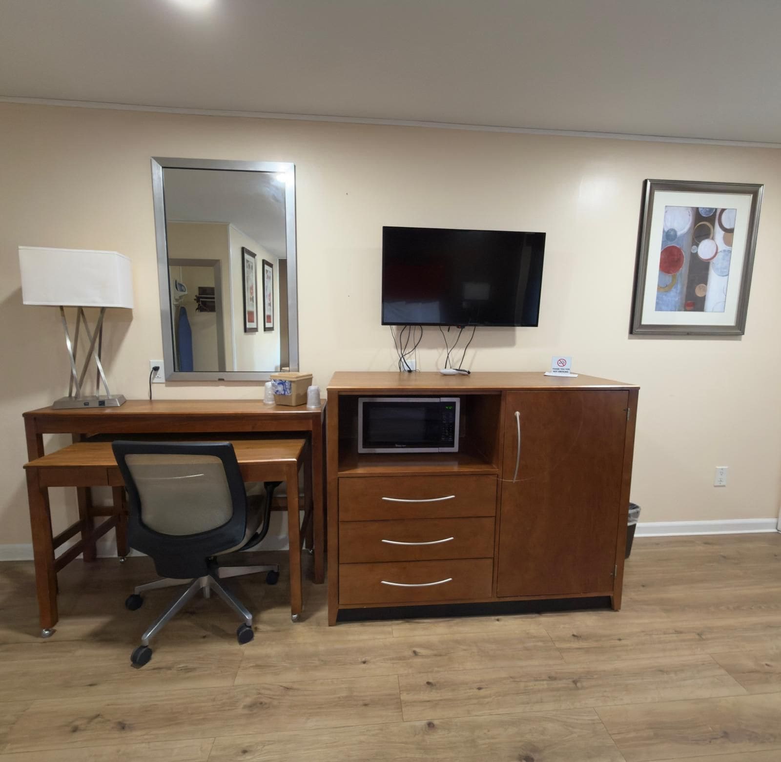 Quarto com escrivaninha de madeira, cadeira, TV de tela plana, micro-ondas e armário.