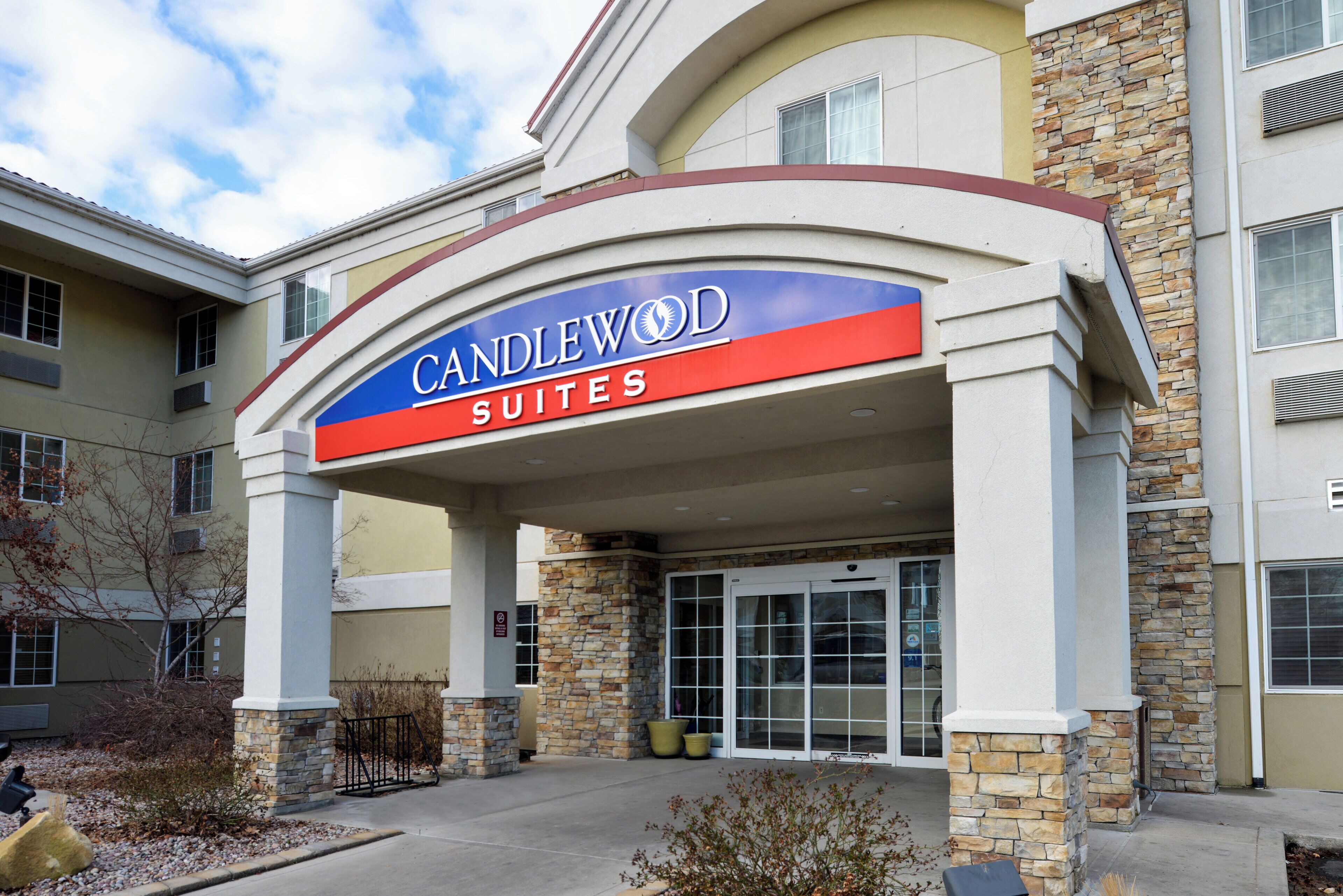 Fachada externa do hotel Candlewood Suites, com revestimento de pedra e placa azul e vermelha.