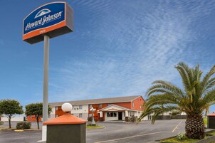 Um hotel Howard Johnson com céu limpo, estacionamento e uma palmeira.