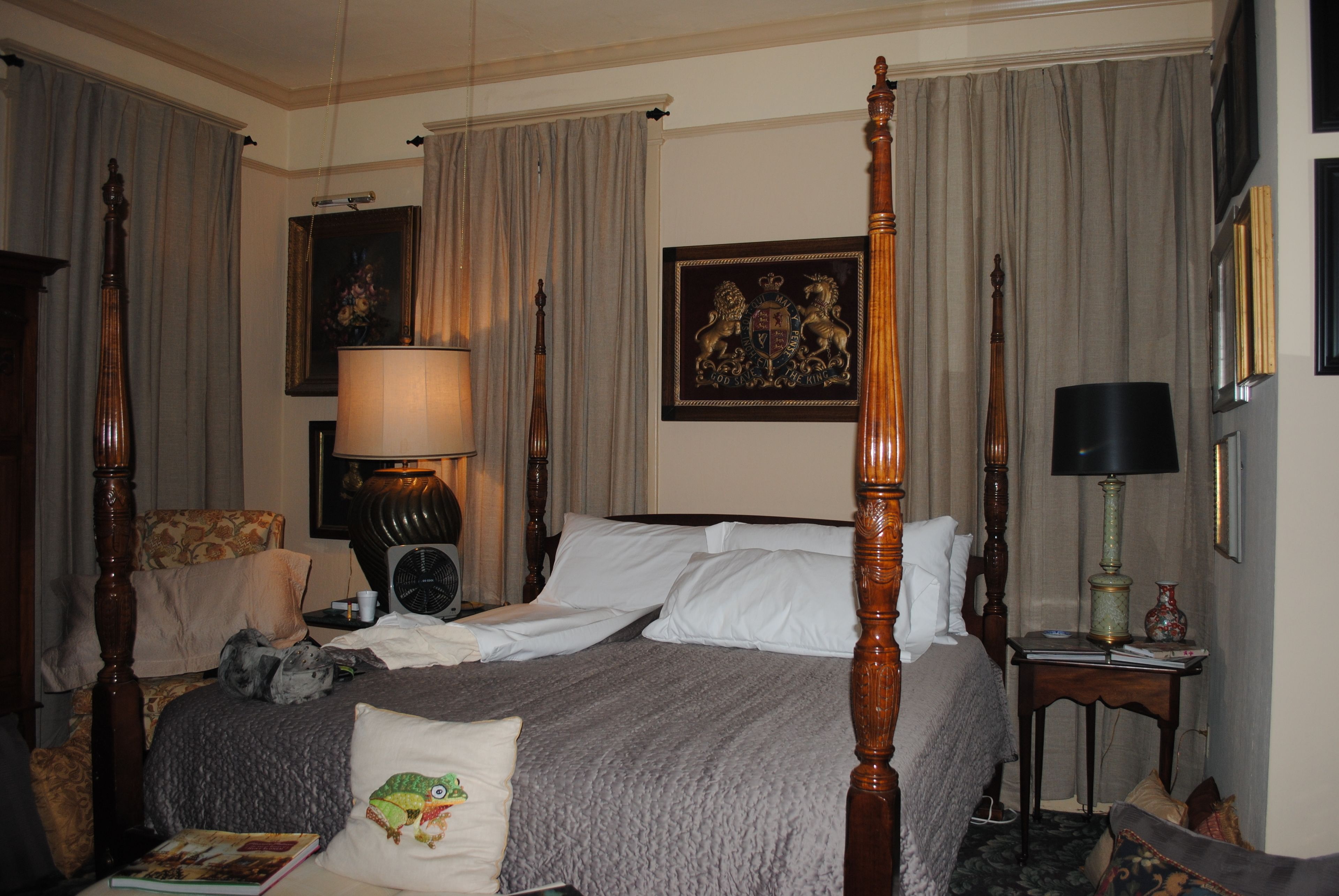 Uma cama de dossel com cabeceira de madeira, uma mesa de cabeceira com abajur e um quadro na parede.
