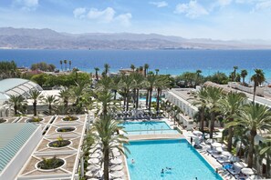 Um resort com uma piscina grande, palmeiras e vista para o mar.