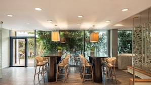 Um interior moderno com uma mesa de jantar central rodeada por cadeiras, janelas amplas com vista para vegetação e iluminação embutida no teto.