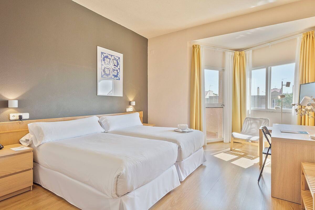 Quarto de hotel com uma cama, mesas de cabeceira, escrivaninha e uma cadeira.