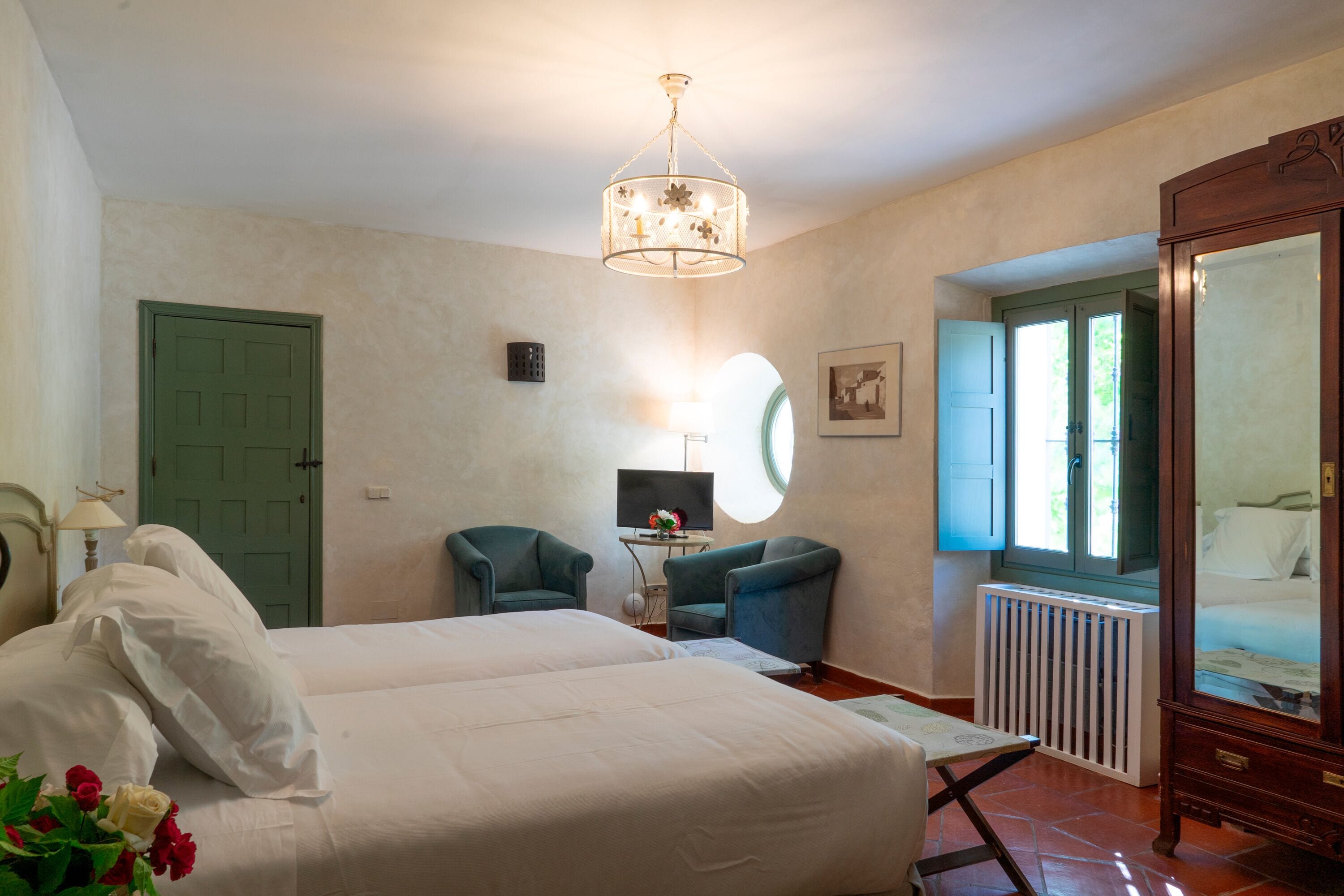 Quarto de hotel com duas camas, um candelabro, uma televisão e um espelho grande.
