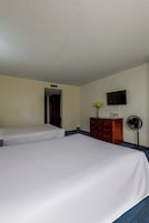 Quarto de hotel com uma cama grande, cômoda, televisão e ventilador.