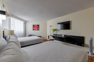 Quarto de hotel com duas camas, uma escrivaninha, uma cadeira, uma televisão e uma janela com cortinas.