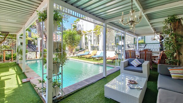 Uma área externa coberta com piscina, espreguiçadeiras e um espaço de estar com almofadas e mesa.