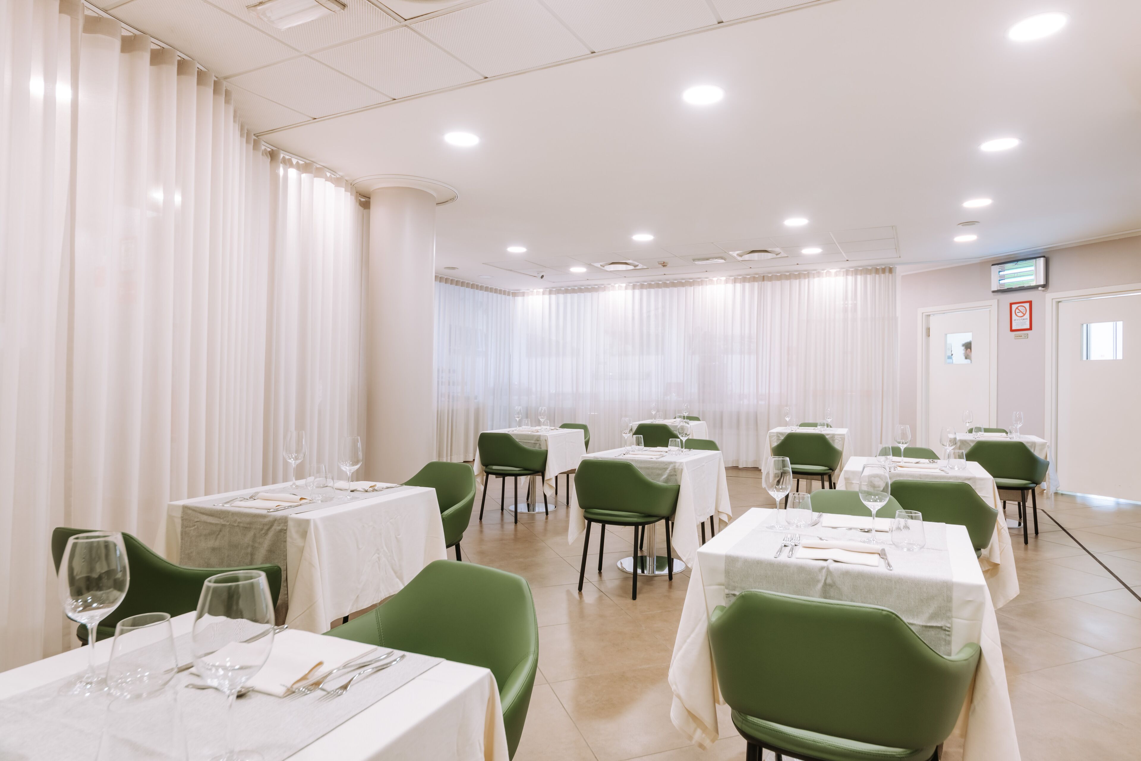 Uma área de refeições com mesas postas, cadeiras verdes e toalhas de mesa brancas.
