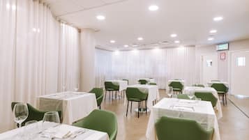 Uma área de refeições com mesas postas, cadeiras verdes e toalhas de mesa brancas.