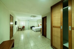 Quarto de hotel com cama, escrivaninha, cadeira, banco e guarda-roupa.