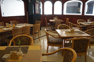 Um restaurante com mesas e cadeiras de madeira, janelas amplas e piso revestido de azulejos.