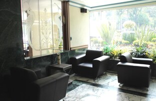 Um hall de entrada com piso de mármore, cadeiras de couro preto, divisória de vidro com desenhos decorativos e vista para um jardim através de grandes janelas.