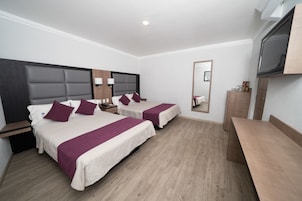 Quarto de hotel com duas camas, uma secretária de madeira, um espelho e uma televisão.