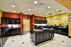 Uma cozinha de hotel com uma ilha central, armários pretos e um relógio na parede.