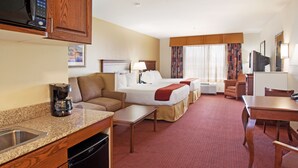 Quarto de hotel com cozinha compacta, cama, sofá, mesa de jantar e televisão.