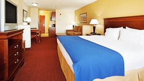 Quarto de hotel com uma cama grande, uma escrivaninha com televisão, uma cadeira e um abajur.