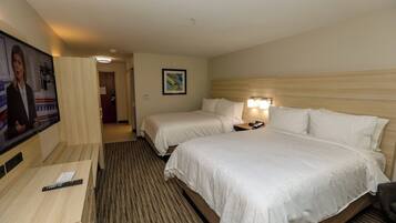 Quarto de hotel com duas camas, uma escrivaninha com televisão e um quadro na parede.
