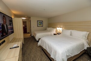 Quarto de hotel com duas camas, uma escrivaninha com televisão e um quadro na parede.