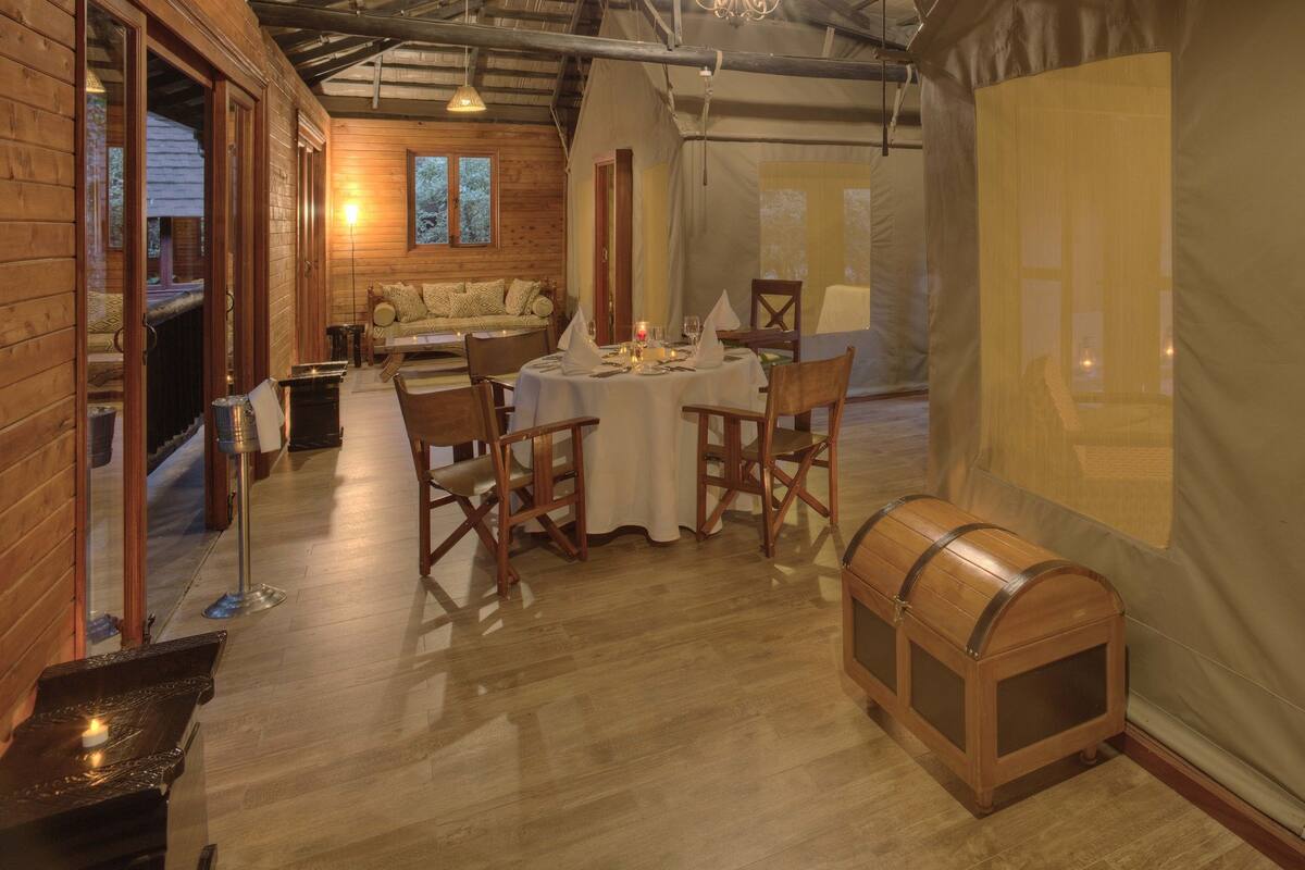 Um quarto aconchegante com piso de madeira, uma mesa de jantar posta para dois, um sofá e uma cama com tapete estampado.