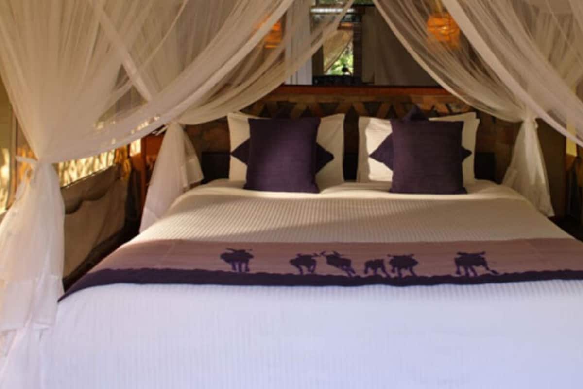 Uma cama com dossel, almofadas e um cobertor com estampas de silhuetas de animais.