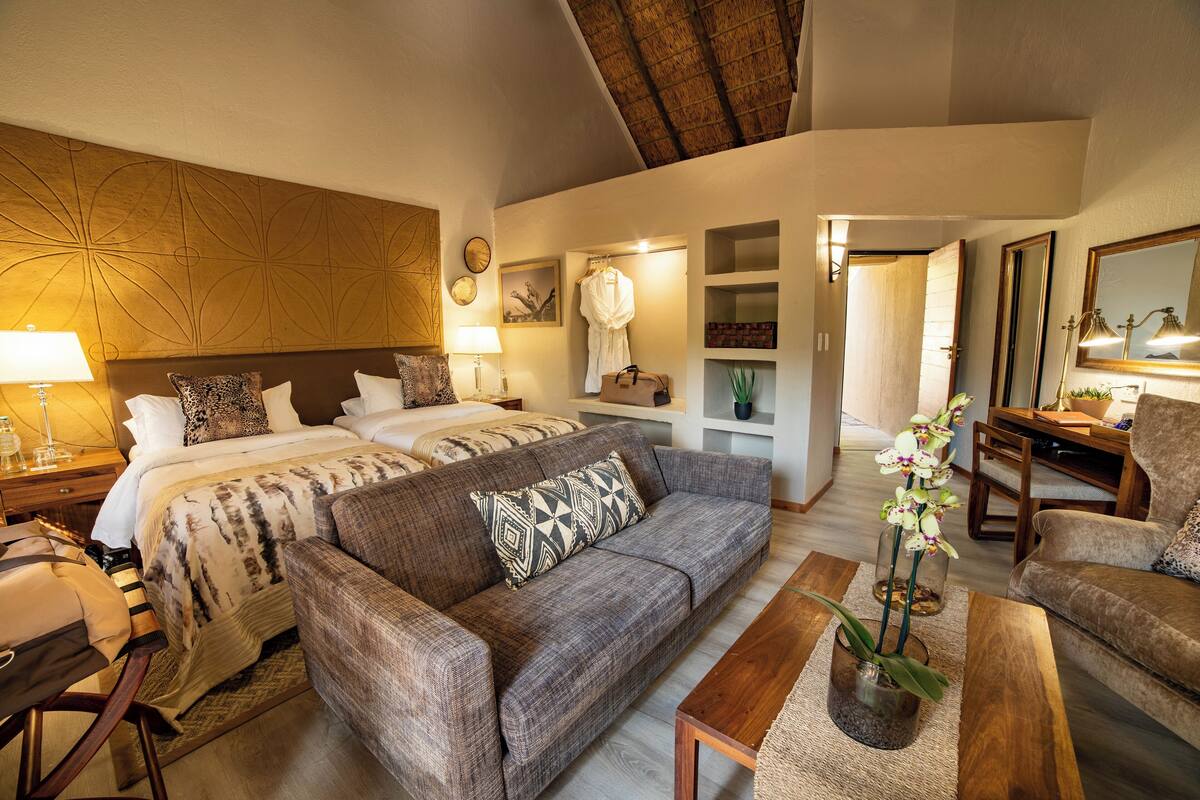 Quarto de hotel com uma cama grande, um sofá, uma mesa de centro e um espelho.