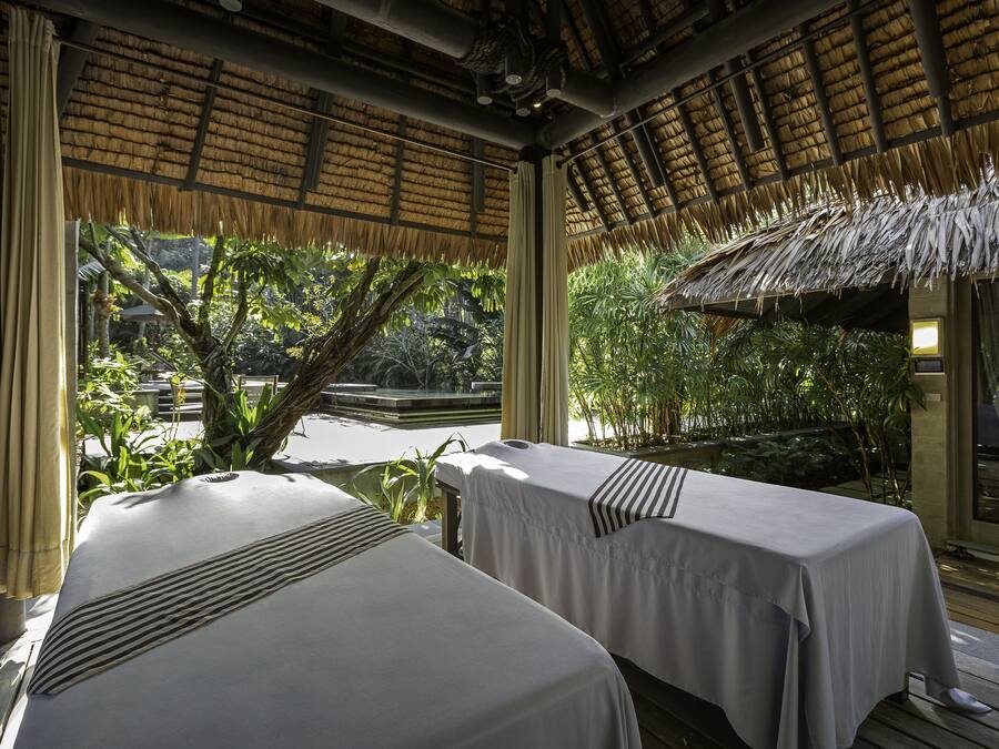 Quarto com duas camas, telhado de palha e amplas janelas com vista para um jardim.