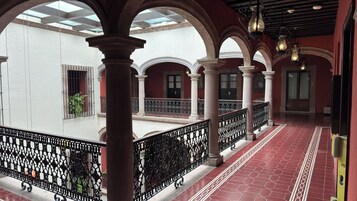Um espaço ao ar livre coberto com piso de telhas vermelhas, colunas brancas e grades de ferro forjado preto.